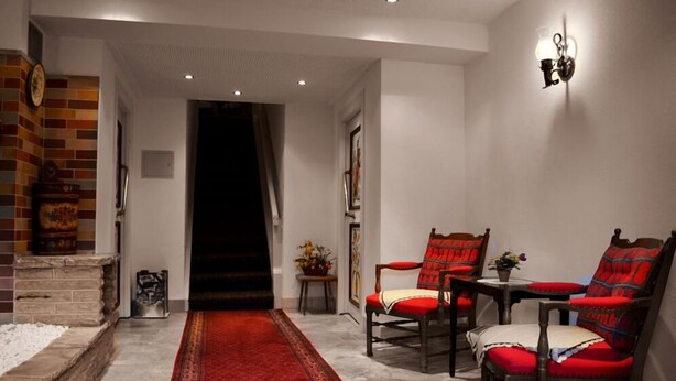 Um corredor com tapete vermelho que leva a uma área de jantar com duas cadeiras de madeira e uma mesa.