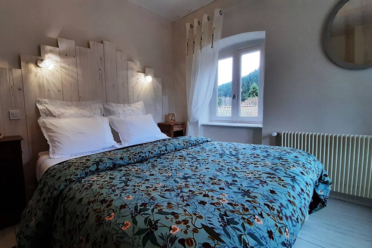 Quarto com cama, mesa de cabeceira, janela e radiador.