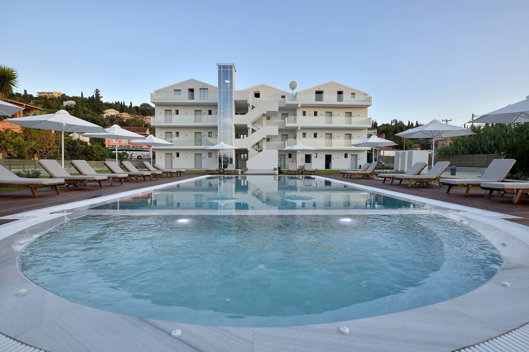 Piscina com espreguiçadeiras e guarda-sóis, rodeada por um edifício moderno com vários andares e varandas.
