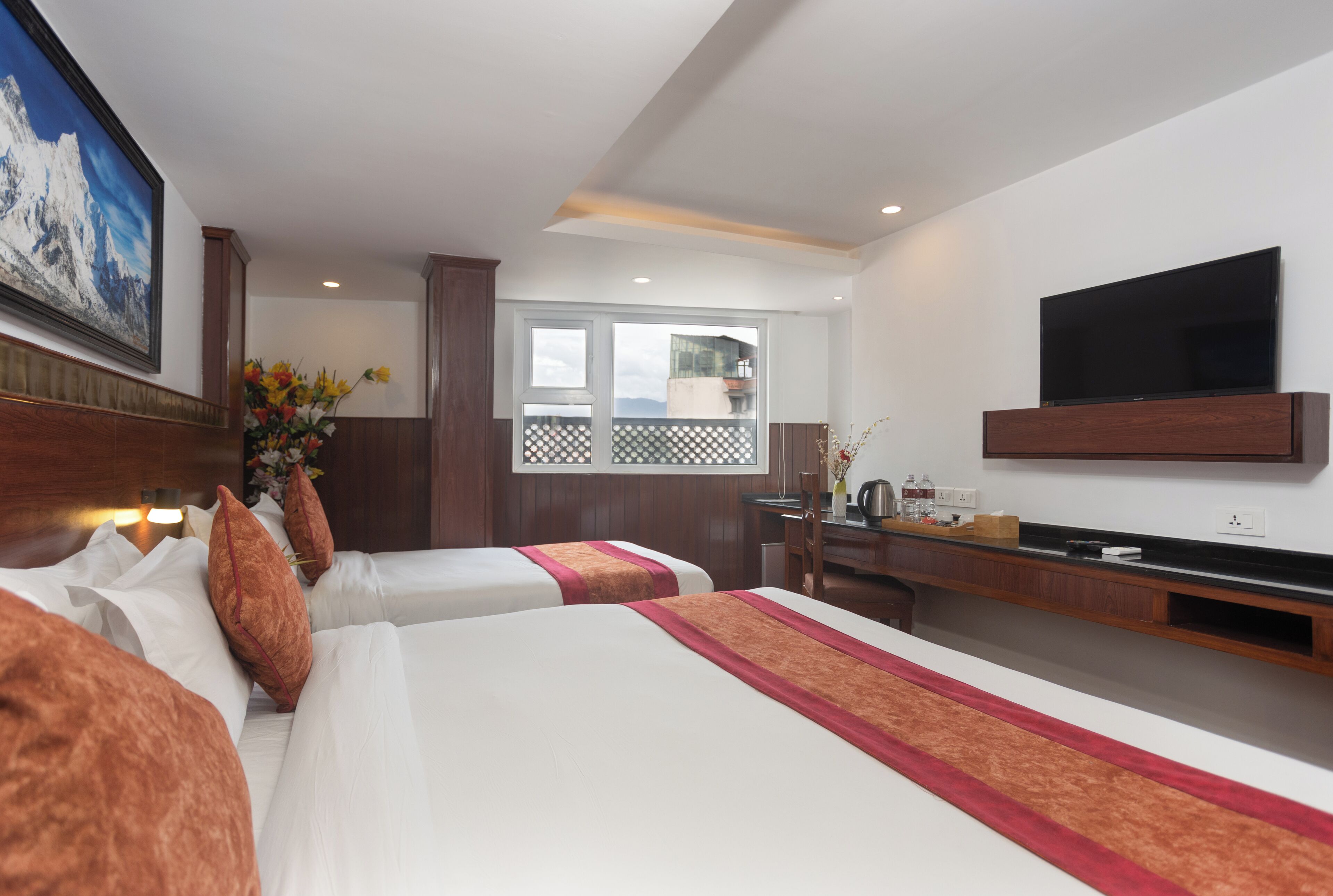 Quarto de hotel com duas camas, televisão, escrivaninha e janela com vista.