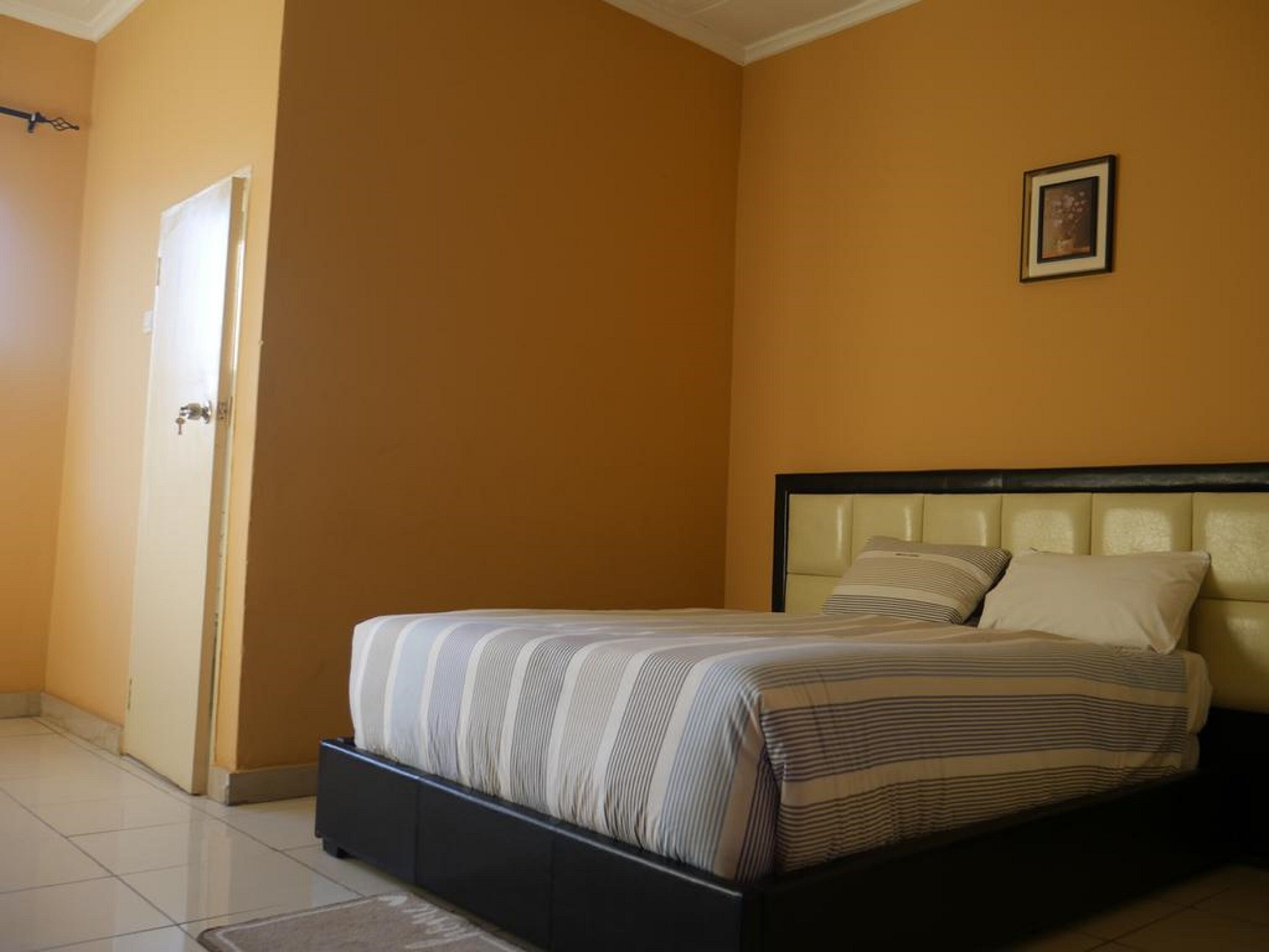 Quarto com cama, porta e quadro na parede.