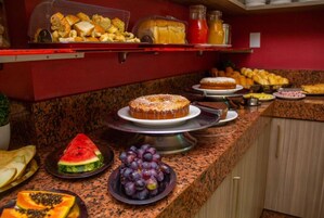 Buffet com diversos alimentos, incluindo bolos, pão e frutas como melancia e uvas.