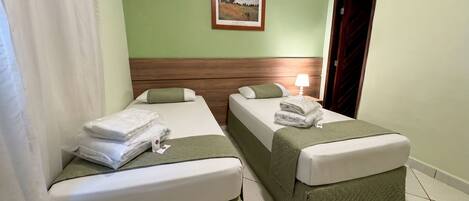 Quarto de hotel com duas camas, um quadro na parede e uma porta à direita.