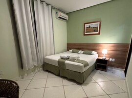 Uma cama bem arrumada com cabeceira verde, uma mesa de cabeceira com abajur e um quadro na parede.