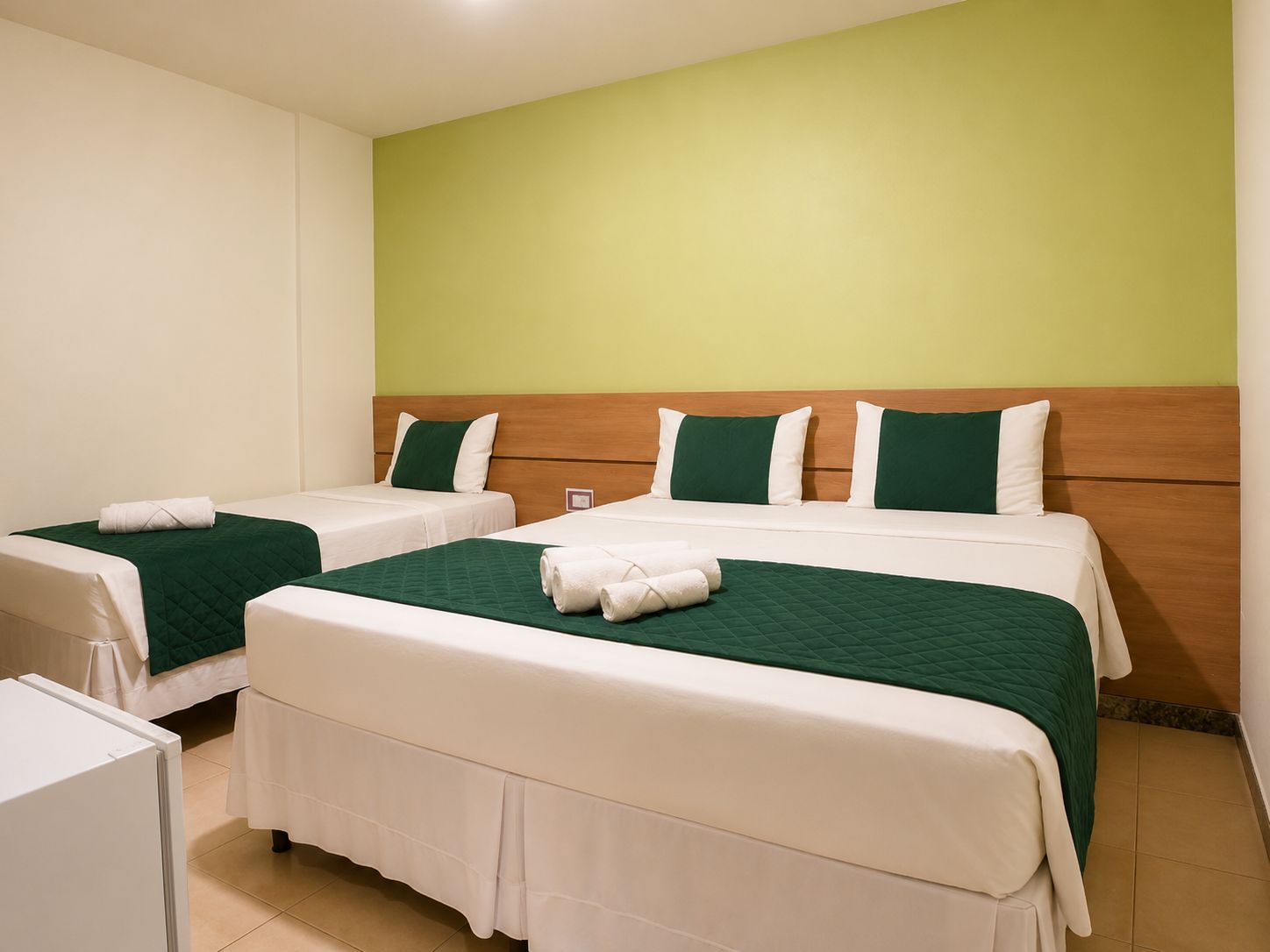 Quarto de hotel com duas camas, cabeceira de madeira e parede verde.