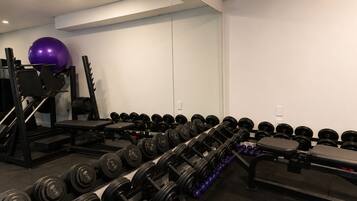 Uma academia com equipamentos de musculação, halteres e uma bola medicinal.