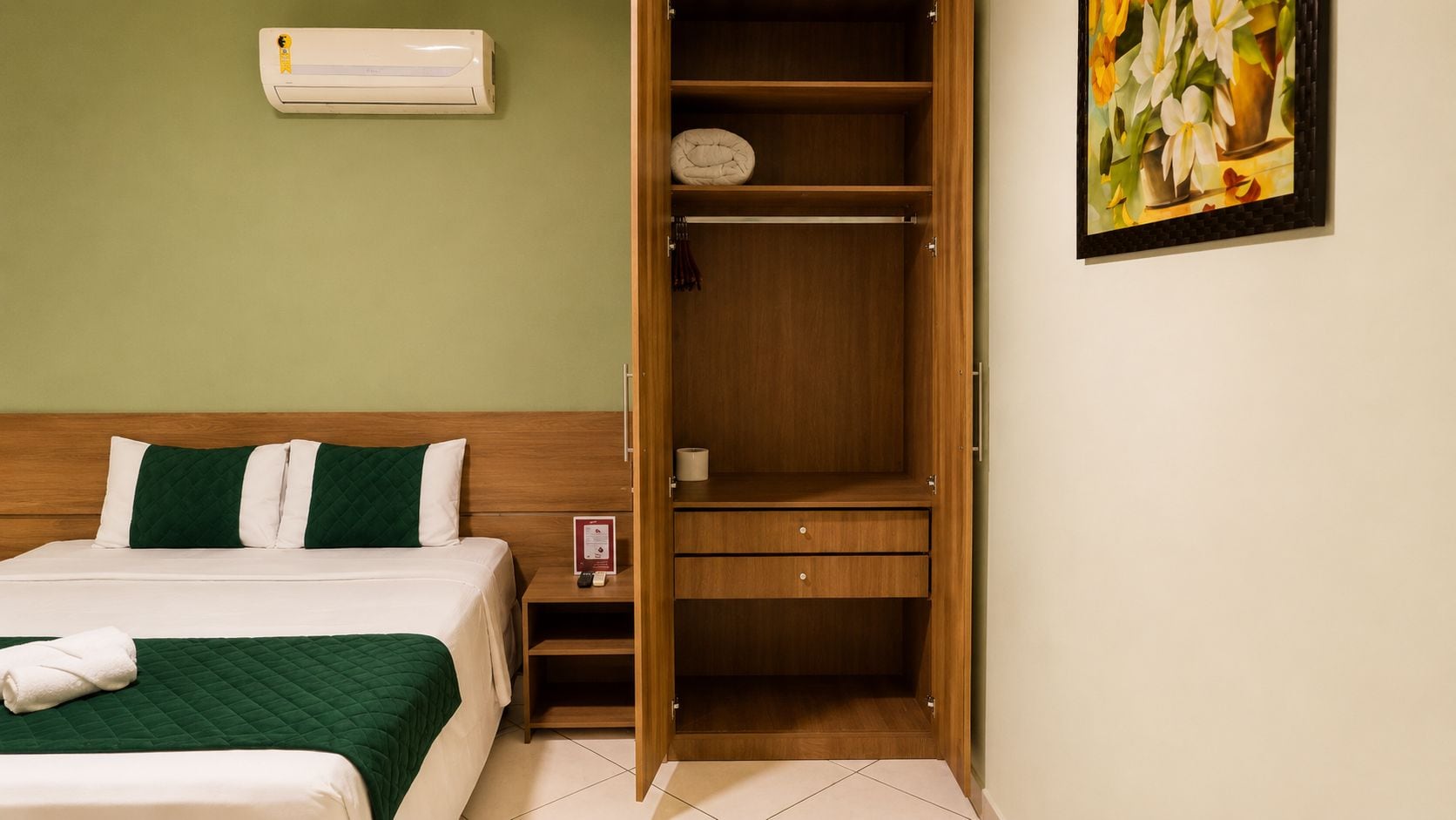 Quarto de hotel com uma cama, guarda-roupa de madeira, quadro na parede e ar condicionado.