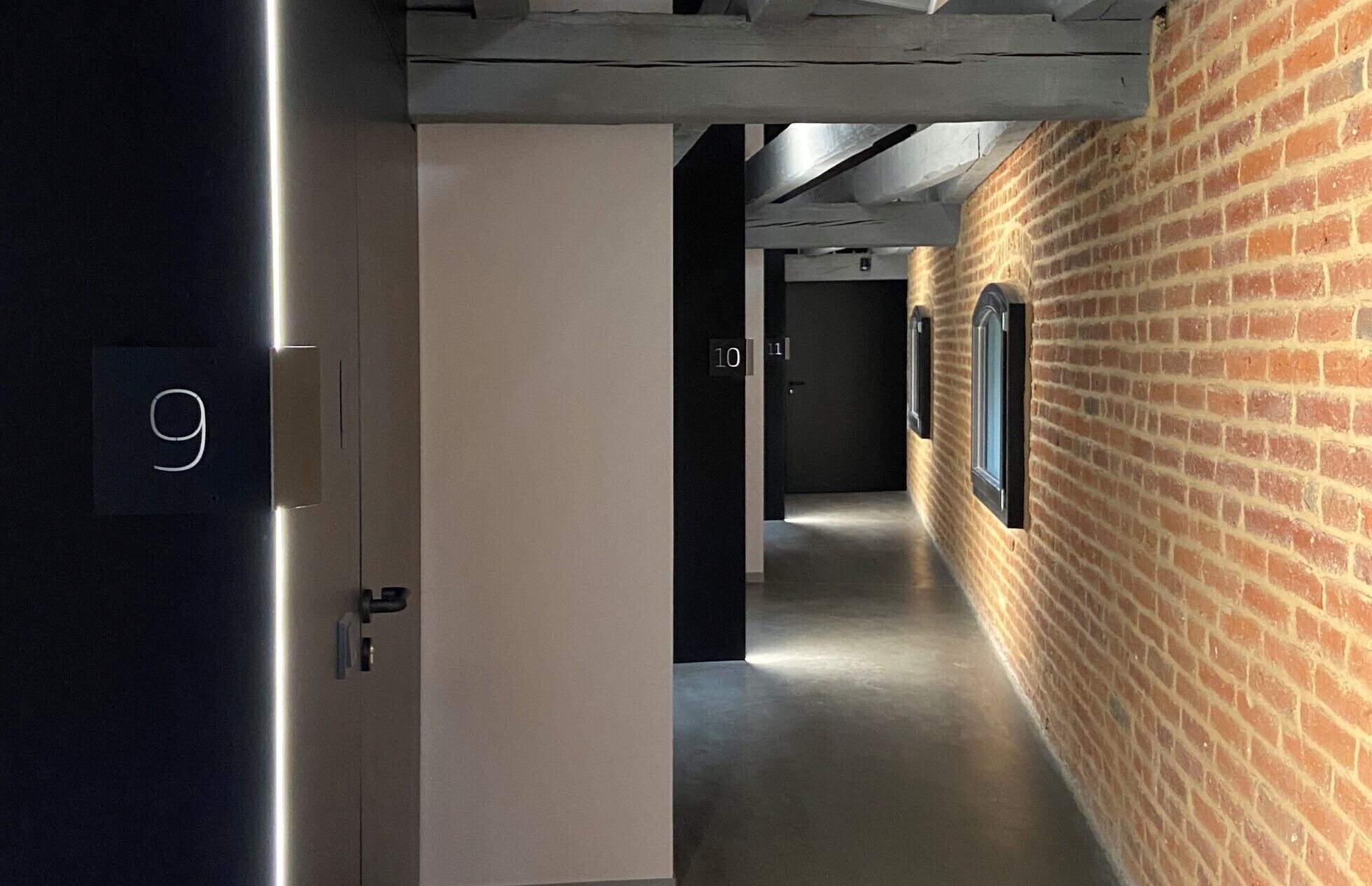 Um corredor com parede de tijolos, uma porta com a inscrição '9' e uma porta com a inscrição '10'.