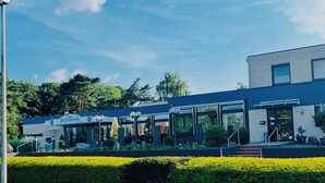 Um edifício moderno com fachada de vidro, uma placa com o nome 'Hans Herrenknecht' e um jardim bem cuidado.