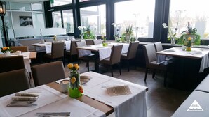 Um restaurante com várias mesas, cada uma com toalhas brancas, cadeiras e louças básicas.