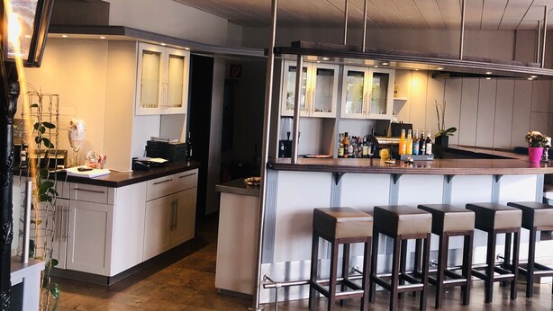 Uma cozinha moderna com armários brancos, um espaço bar com banquetas e um lustre.