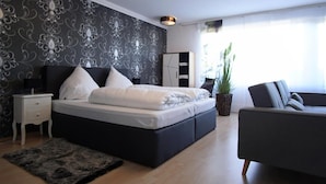 Quarto moderno com uma cama grande, mesas de cabeceira, um guarda-roupa e um sofá.