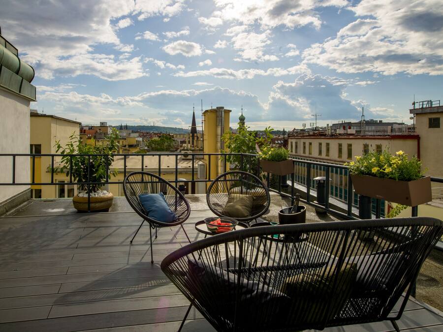 Terraço no telhado com cadeiras de vime, plantas em vasos e vista para a cidade.