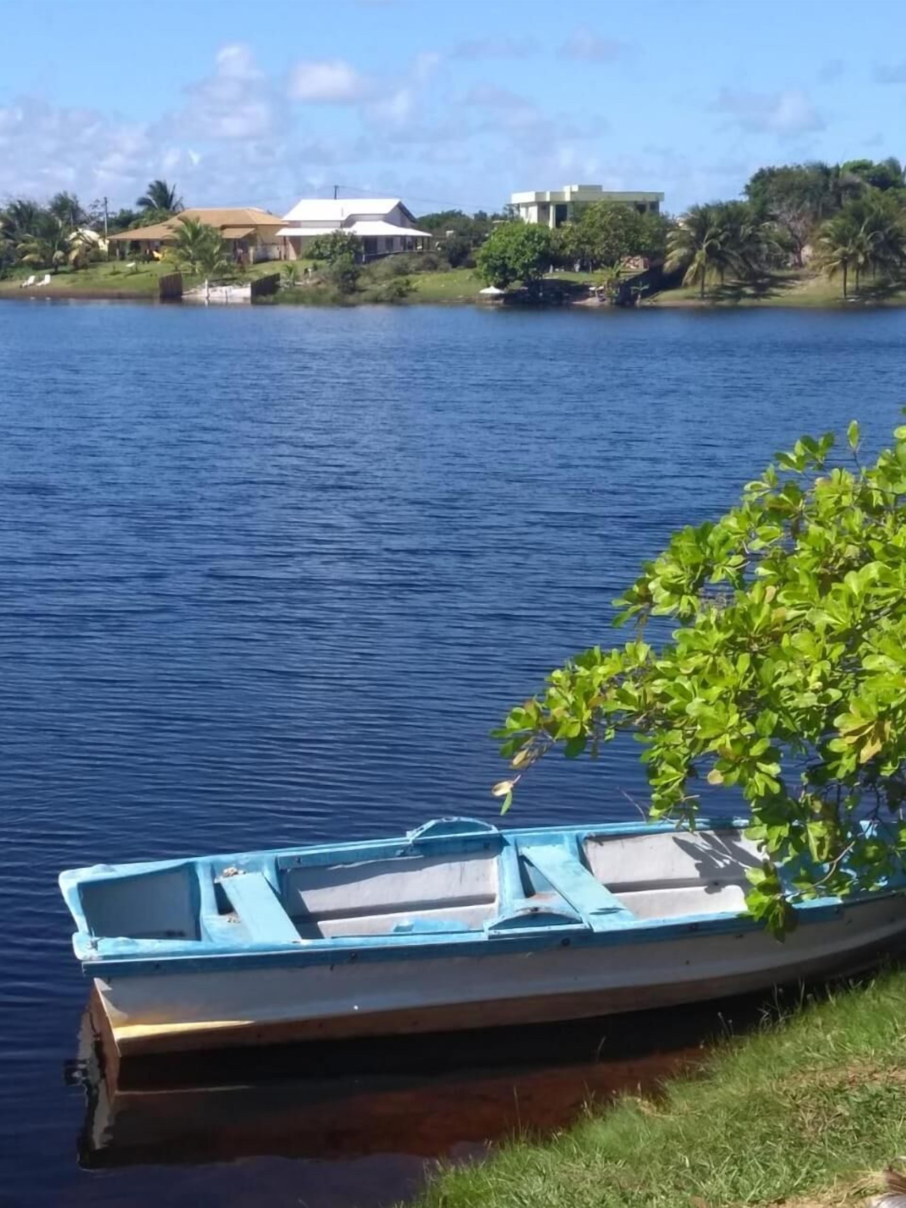 Um barco atracado em um lago calmo, com margem gramada e um edifício ao fundo.