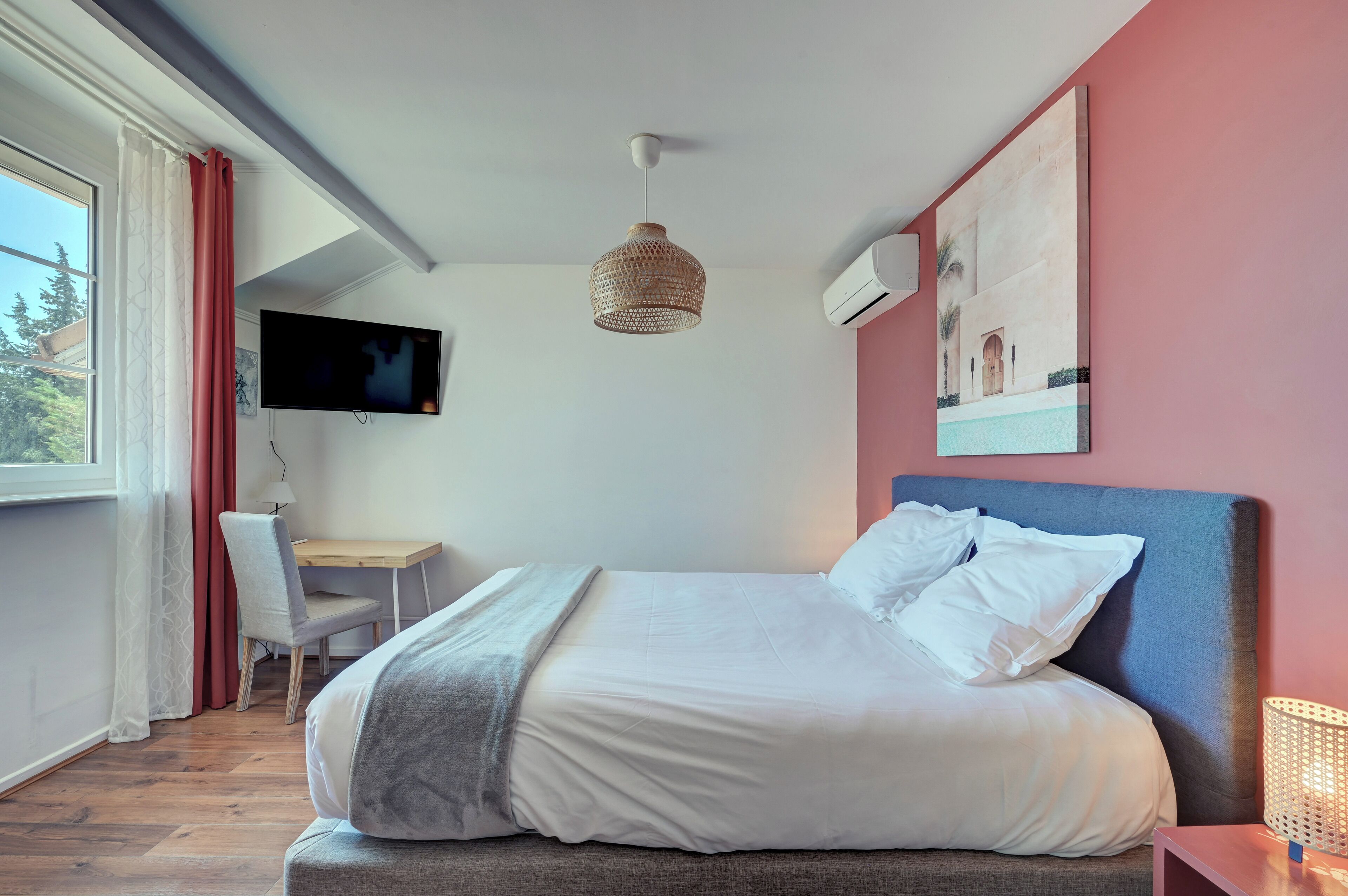 Quarto com cama, escrivaninha, cadeira, televisão e um quadro na parede.