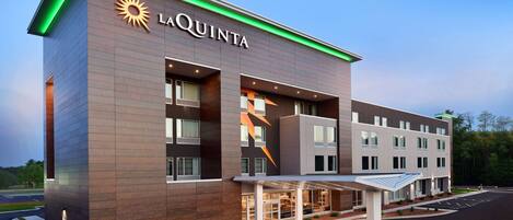 Um hotel La Quinta com design moderno, apresentando um sol em destaque no logotipo, uma entrada coberta e um estacionamento.
