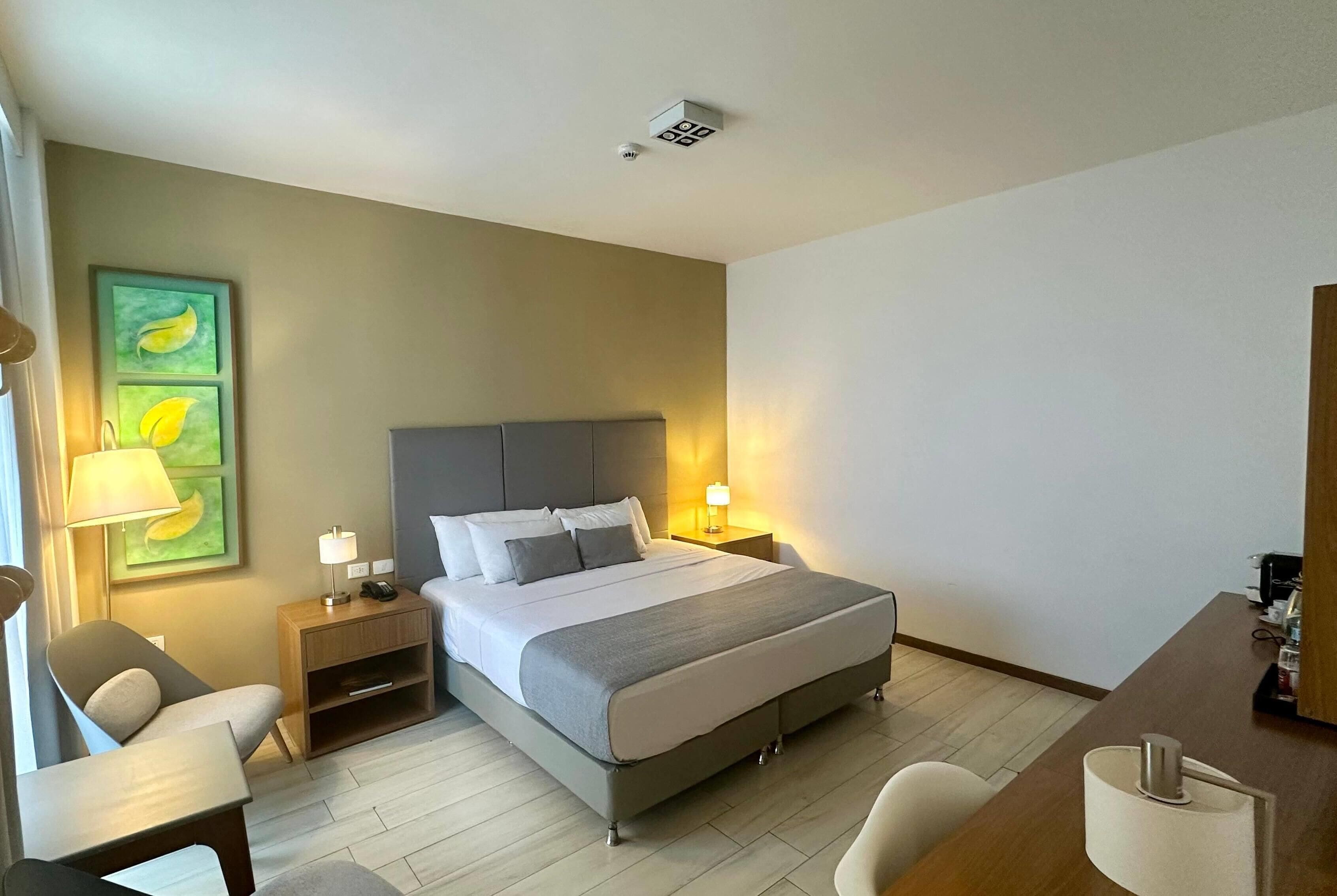 Quarto de hotel moderno com uma cama grande, mesas de cabeceira, uma escrivaninha e uma cadeira.