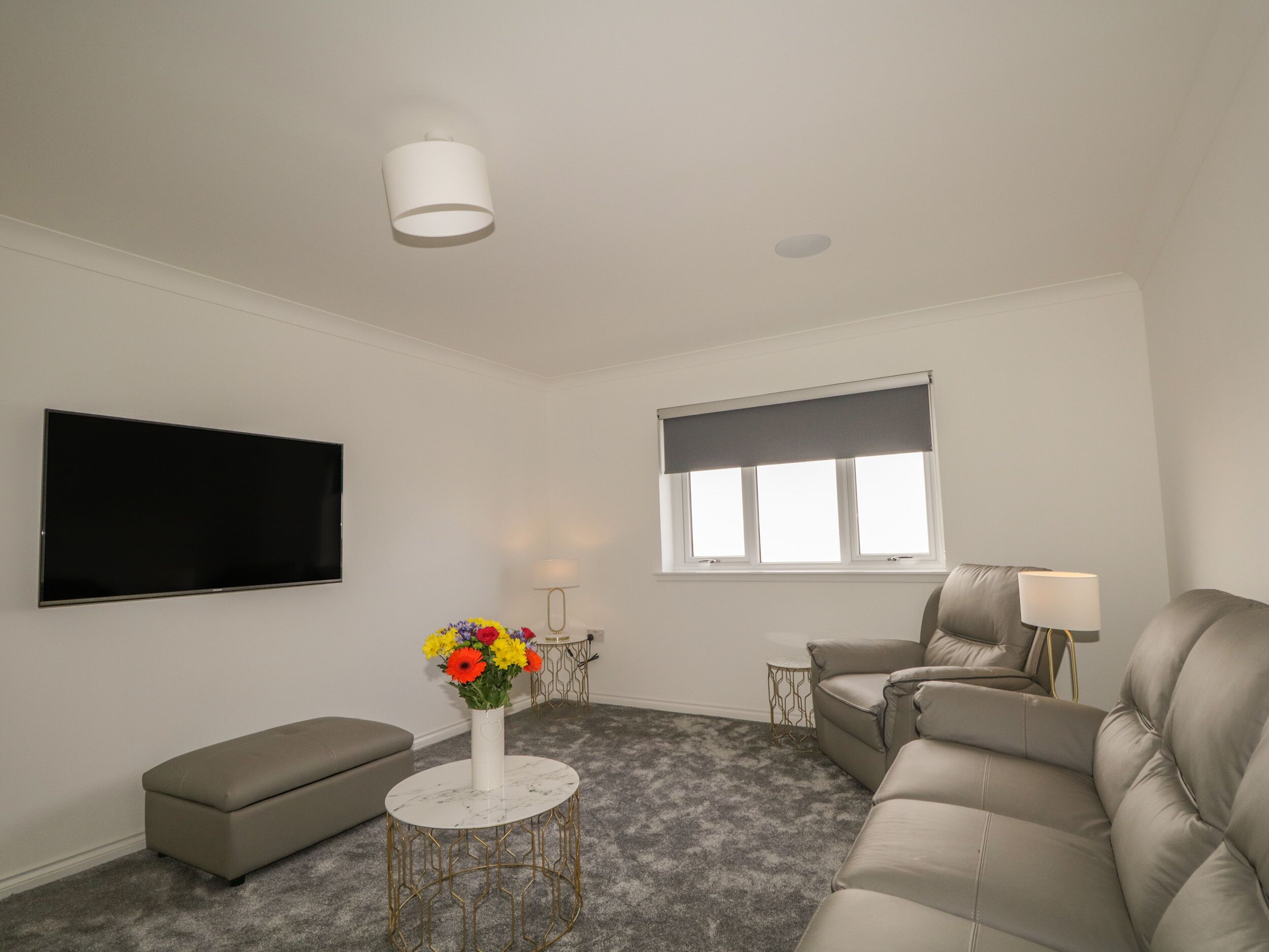 Uma sala de estar moderna com uma televisão de tela plana, um sofá, um bicomodo, uma mesa de centro redonda e um vaso com flores.