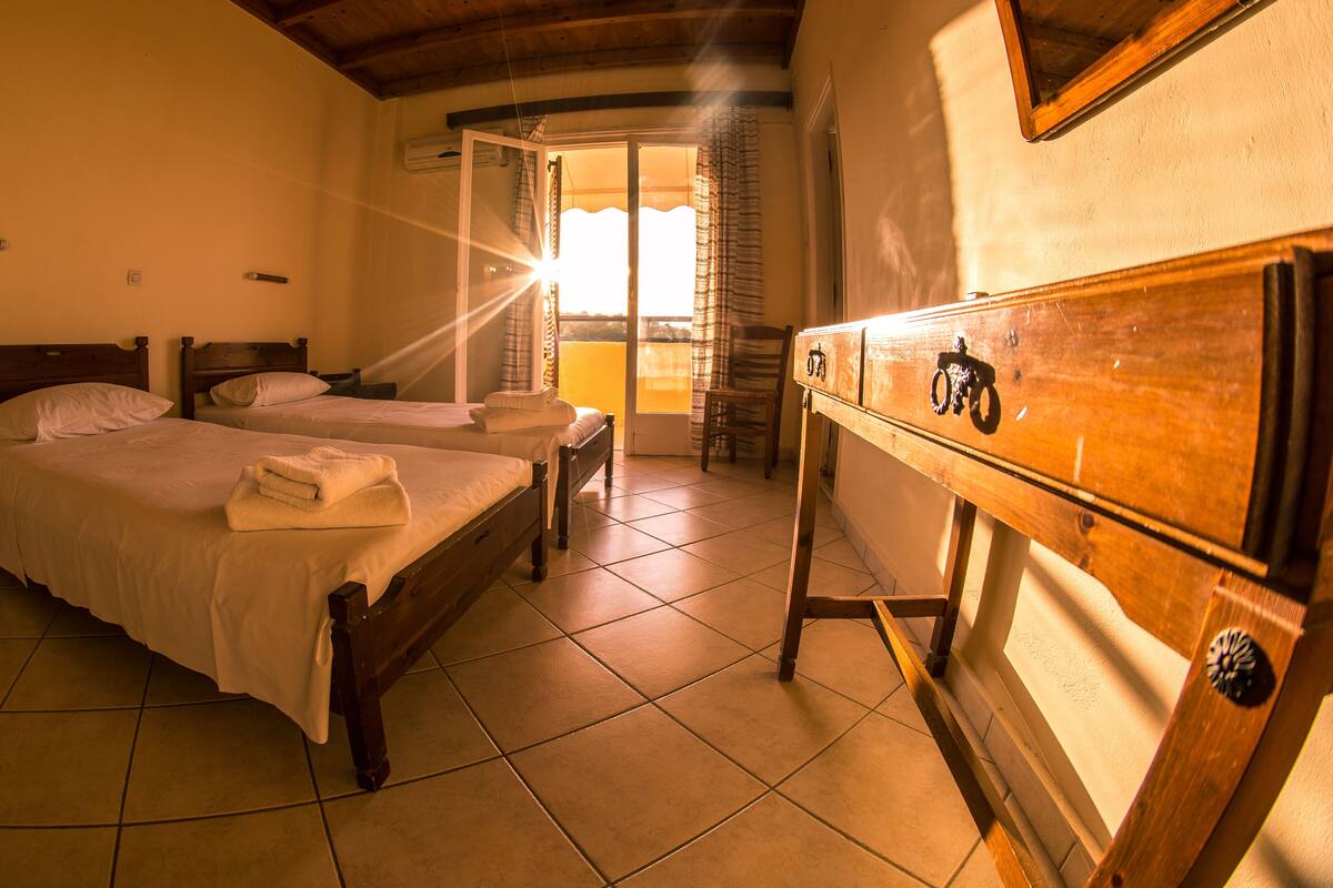 Quarto de hotel com duas camas de madeira, uma cômoda de madeira e uma varanda com vista.