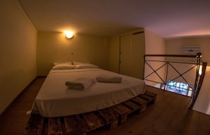 Quarto com cama, um banco de madeira, escadas e vista pela janela.