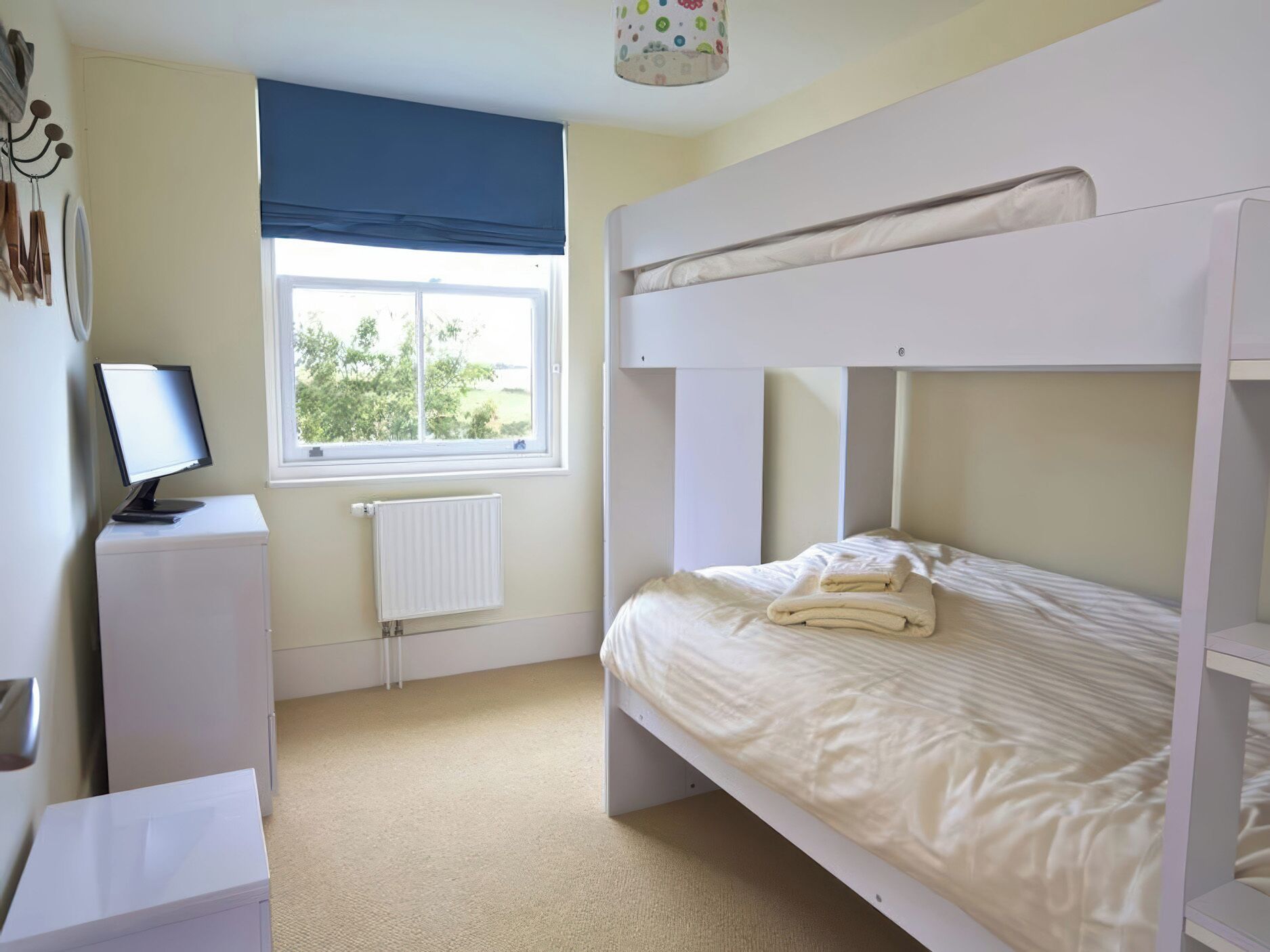 Quarto com beliches, uma escrivaninha com computador, janela com vista para o verde e um radiador.