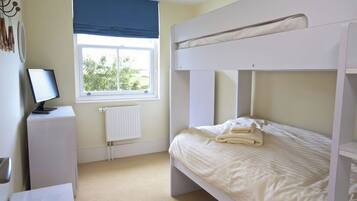 Quarto com beliches, uma escrivaninha com computador, janela com vista para o verde e um radiador.
