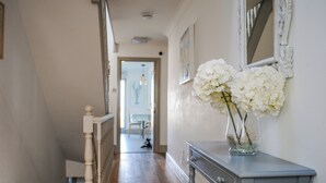 Um corredor com piso de madeira, corrimão branco e um console cinza com um vaso de flores brancas.