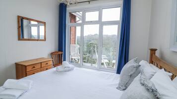 Quarto com cama grande, cómoda de madeira, uma cadeira e varanda com cortinas azuis.