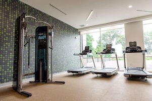 Uma academia com esteiras, aparelho de musculação e amplas janelas.
