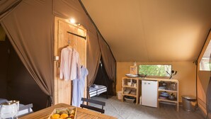 Alojamento com tenda, mesa de madeira, cesta de frutas, cama, pequeno kitchenette e um cabideiro.