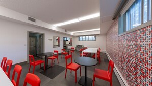 Uma sala de conferências com cadeiras e mesas vermelhas, uma pequena cozinha e um painel de parede com padrão.