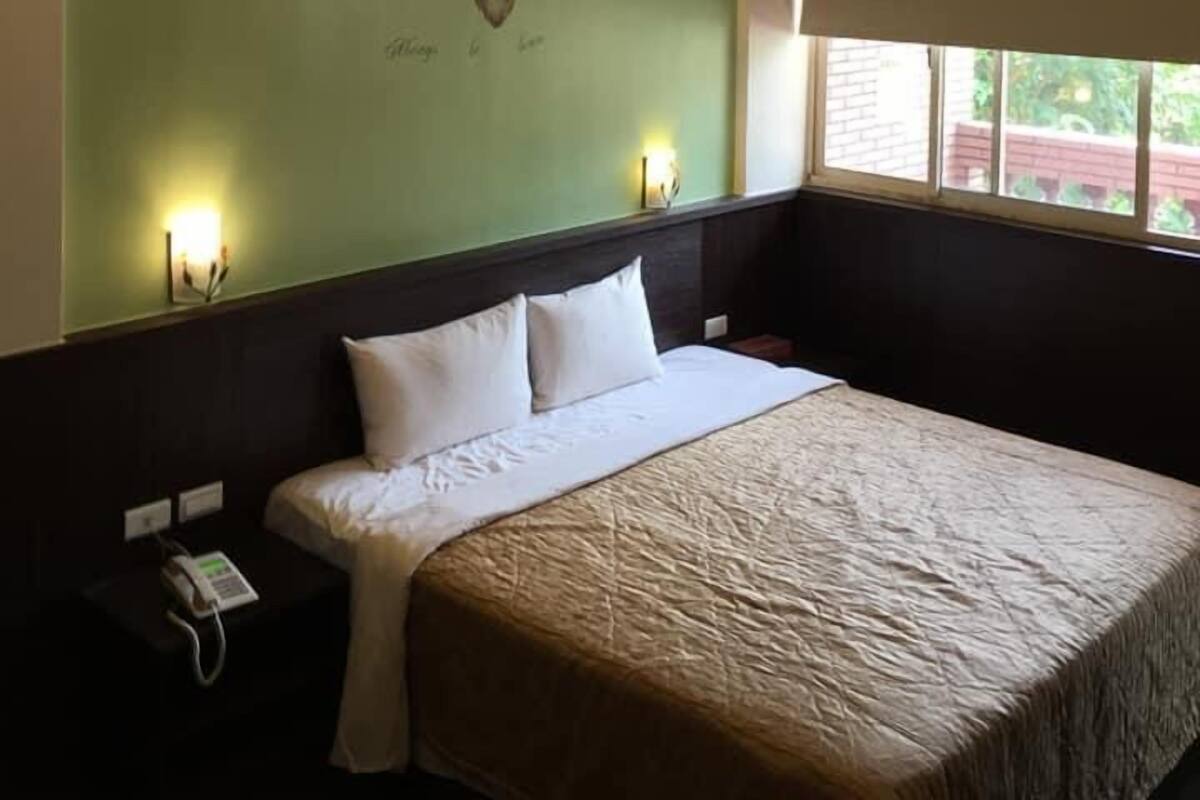 Quarto de hotel com cama, mesa de cabeceira e parede com pintura de uma árvore.