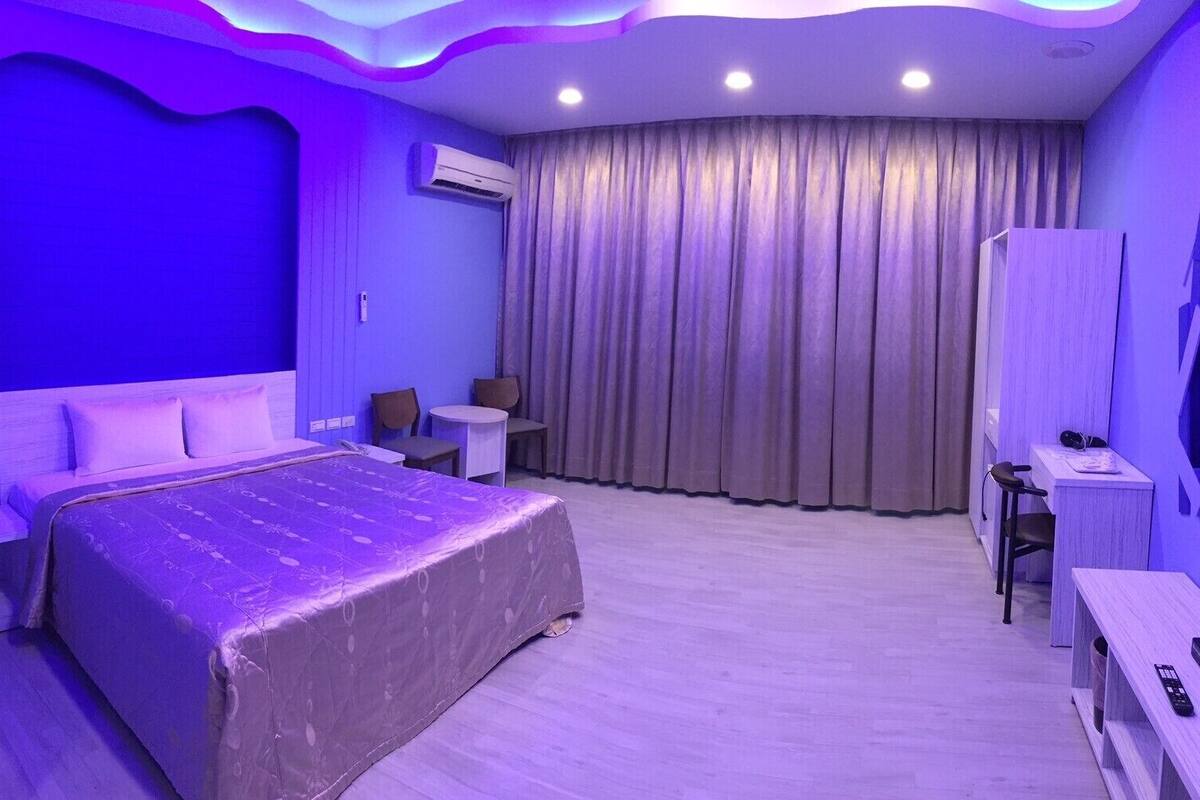 Quarto de hotel com uma cama grande, uma escrivaninha, uma cadeira, uma mesinha de apoio e um guarda-roupa.