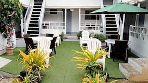 Um pátio com escadaria central, cadeiras brancas e plantas em vasos.