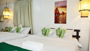 Quarto de hotel com duas camas, uma toalha verde, uma pintura de um veleiro e duas luminárias de parede.