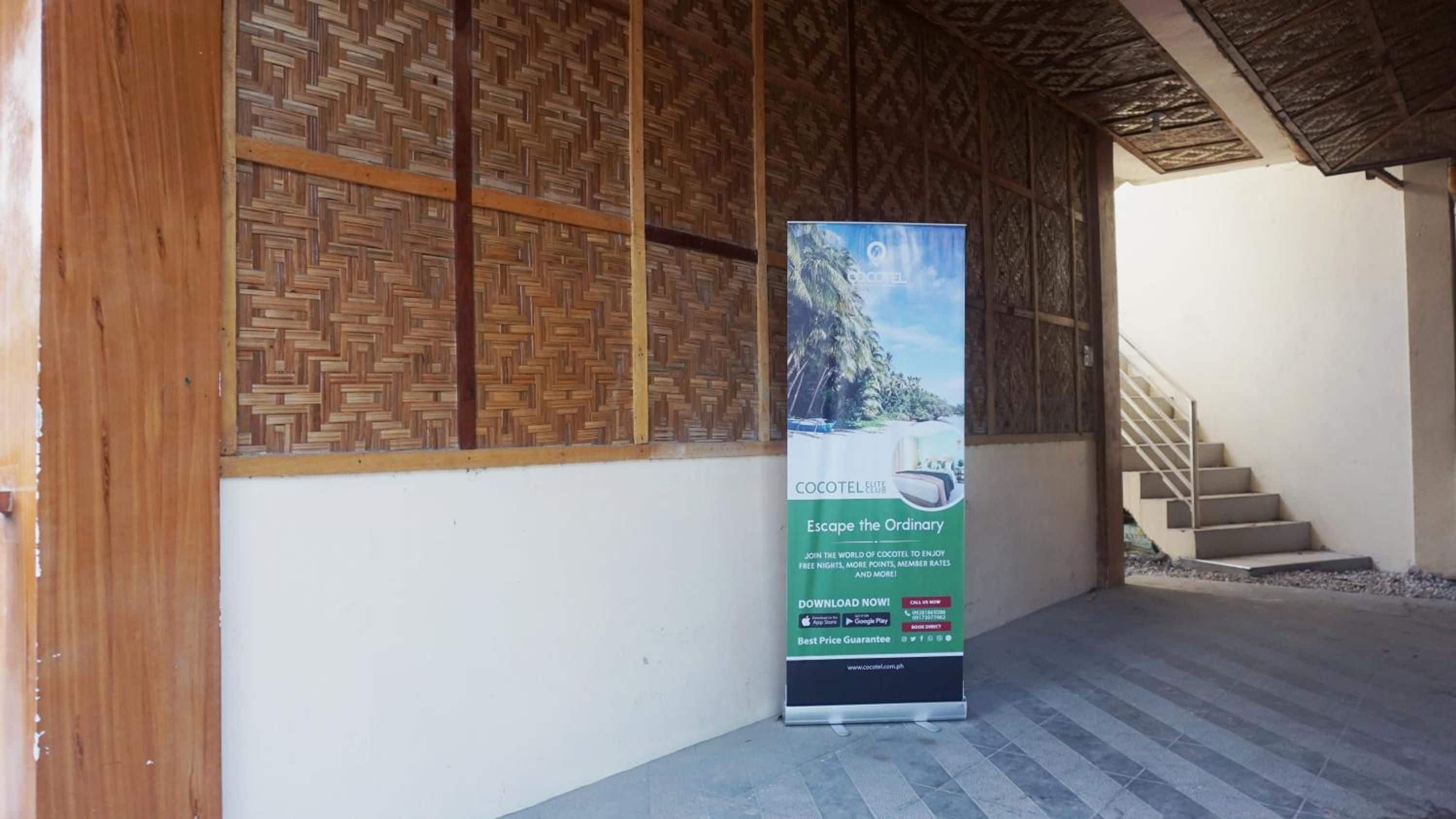 Cartaz promocional do COCOTEL BUREAU em frente a um edifício com parede de bambu trançado e escadaria.
