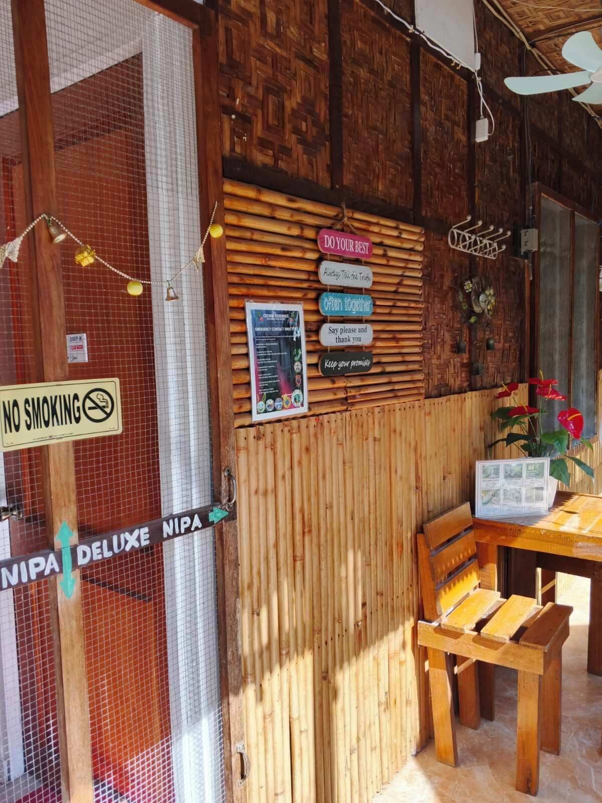 Interior em madeira com placa de proibição de fumar, quadro de menu e área de estar com mesa e cadeiras.
