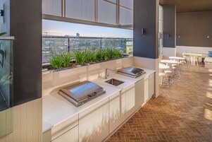 Cozinha moderna com churrasqueira embutida, pia e janela com vista para a paisagem urbana.