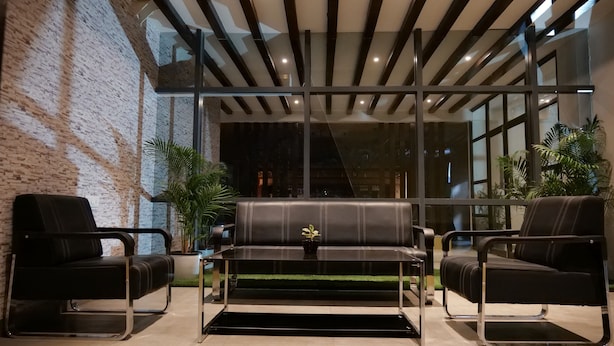 Um hall moderno com parede de vidro, um sofá de couro preto, duas poltronas de couro preto e uma pequena planta no sofá.