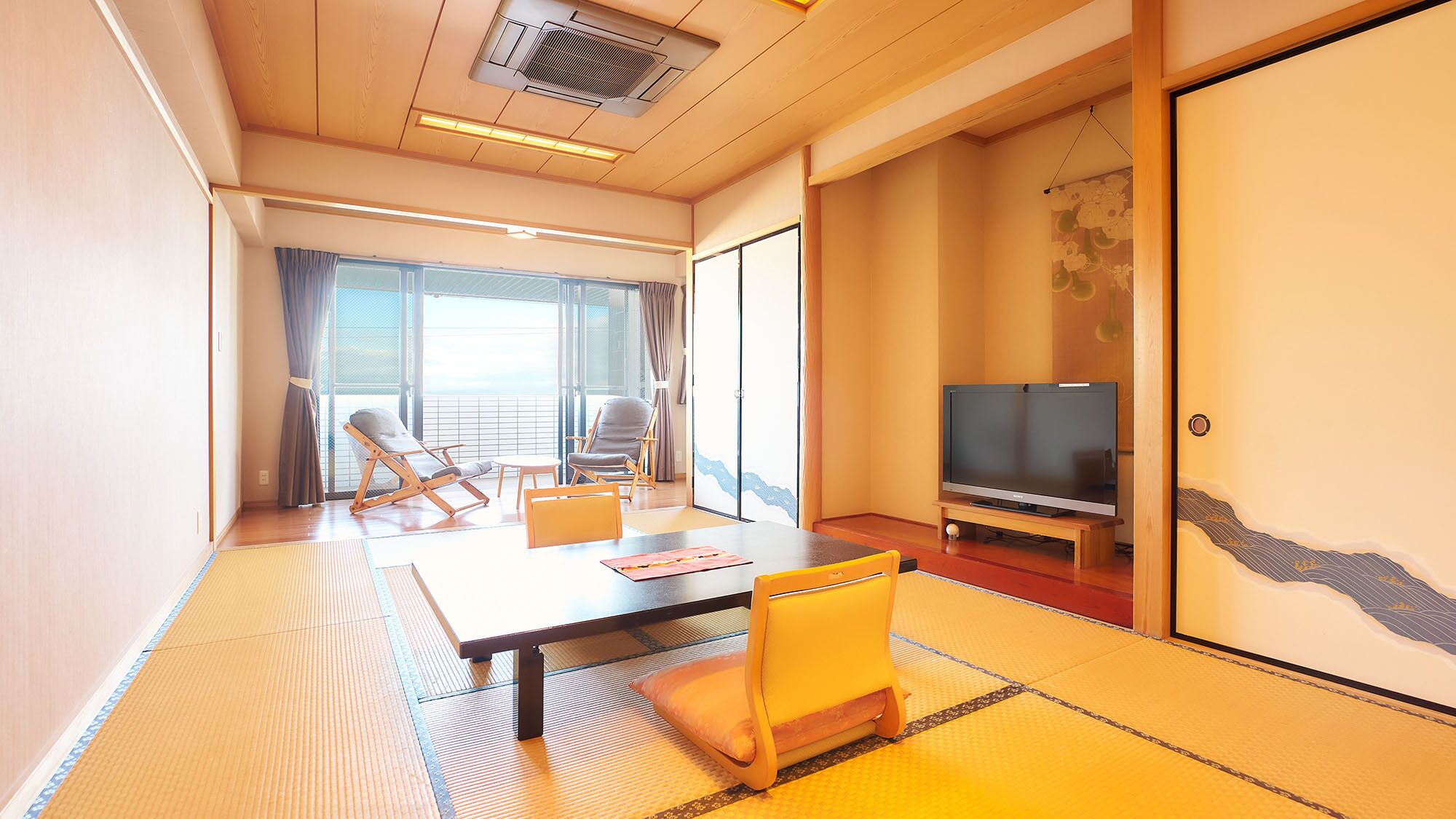 Quarto de hotel com uma grande porta de vidro deslizante, televisão de tela plana, piso de esteira de tatame e porta tradicional japonesa deslizante.