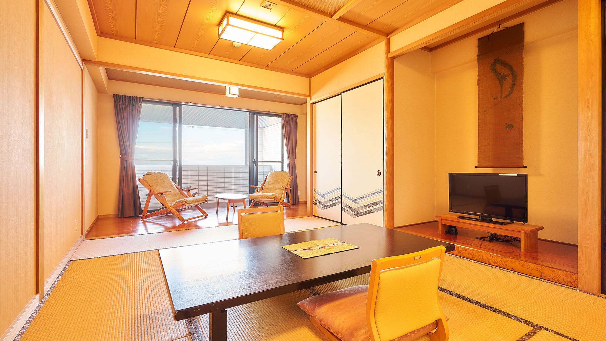 Quarto com piso de madeira, esteira de tatame, televisão e duas cadeiras.