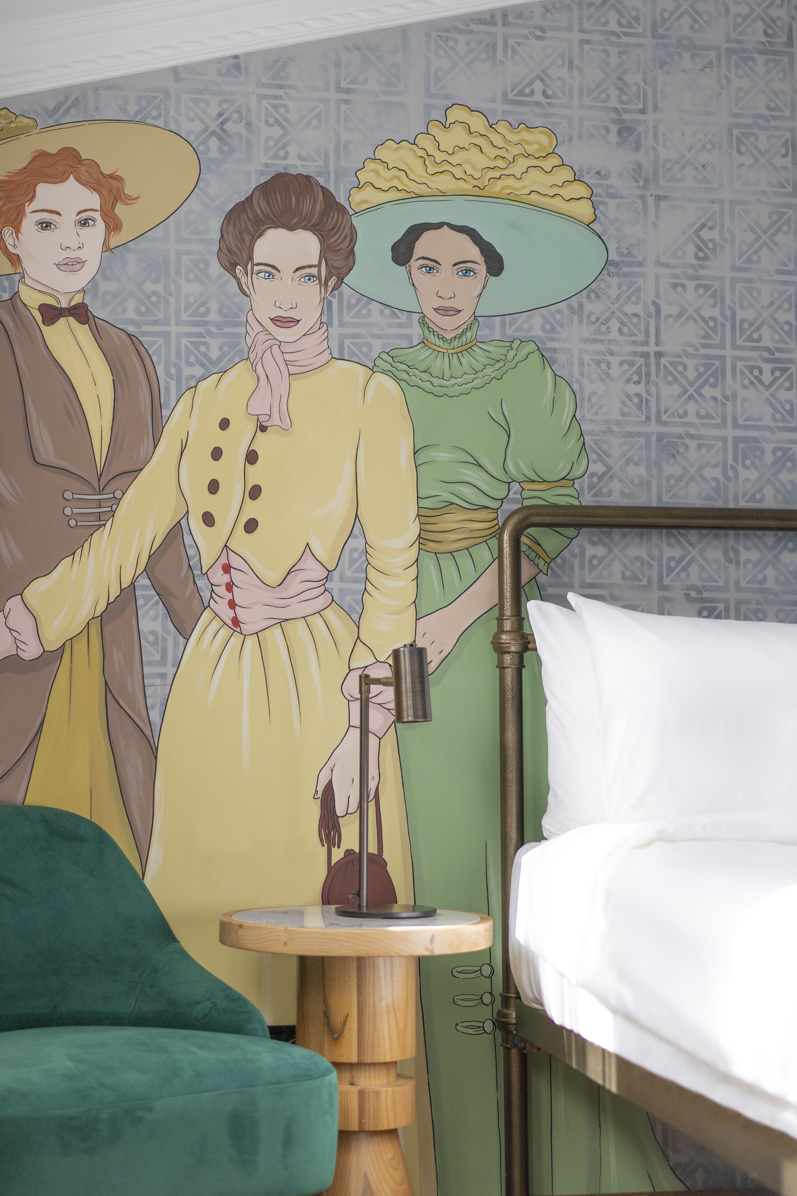 Quarto com uma cama, uma poltrona verde, uma mesinha de cabeceira de madeira e uma parede com papel de parede estampado.