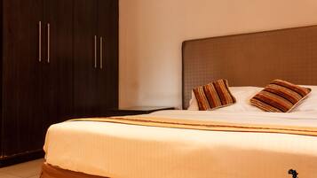 Cama bem arrumada com cabeceira, duas almofadas e um guarda-roupa de madeira escura com puxadores.