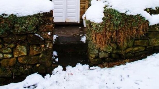 Uma casa de pedra com porta e janelas brancas, rodeada por neve.