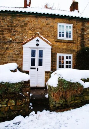 Uma casa de pedra com porta e janelas brancas, rodeada por neve.