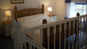 Quarto com cama de madeira, duas mesas de cabeceira com luminárias, um criado-mudo e uma janela com cortinas.