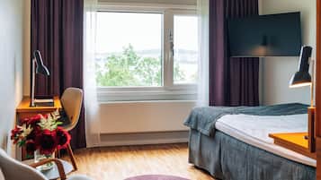 Quarto de hotel com cama, escrivaninha, cadeira, televisão e janela com vista.