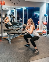 Academia com equipamentos de ginástica, espelho e uma pessoa fazendo agachamentos.
