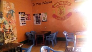 Quarto com paredes laranja, cadeiras de plástico azul, uma mesa e cartazes, incluindo um do Manchester United.