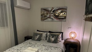 Quarto com cama, ar condicionado fixado na parede, luminária decorativa e um quadro.